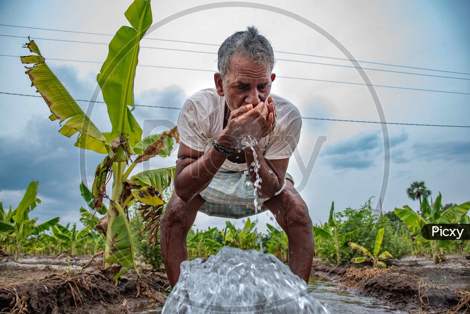 Image of a farmer drinking water from a pumpset in a field-RS367625-Picxy
