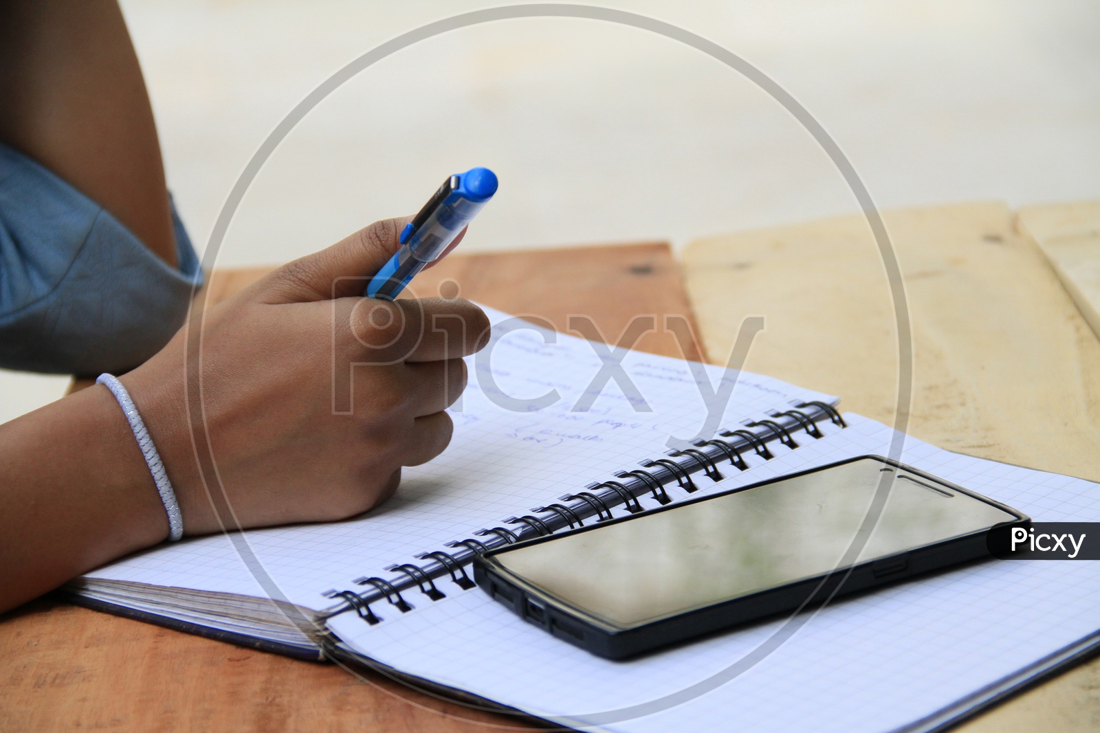 Image of Student Taking Notes In a Notebook And Smartphone on a Wooden ...