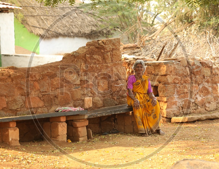 Image of A elderly lady standing beside the brick wall under the tree ...
