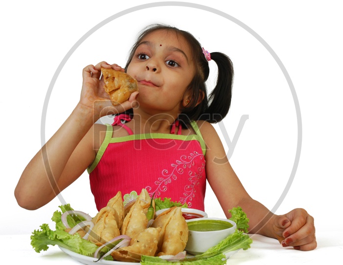 Image of Indian little girl eating samosa-HM752357-Picxy