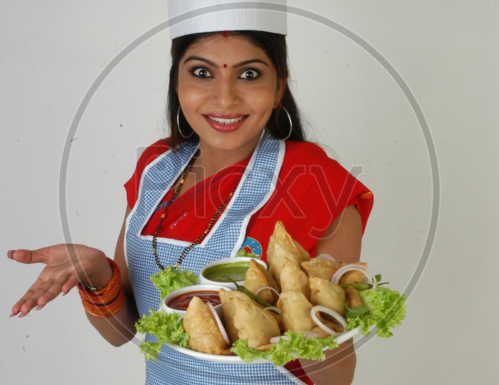 Image of An Indian Woman Chef In Kitchen Apron And Cap Holding Samosas ...