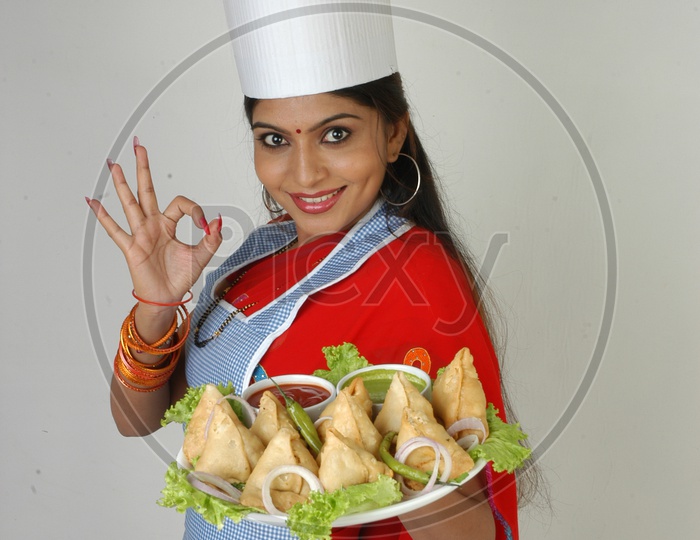 Image of An Indian Woman Chef In Kitchen Apron And Cap Holding Samosas ...