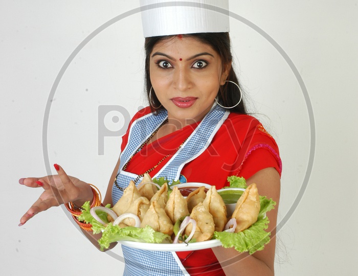 Image of An Indian Woman Chef In Kitchen Apron And Cap Holding Samosas ...