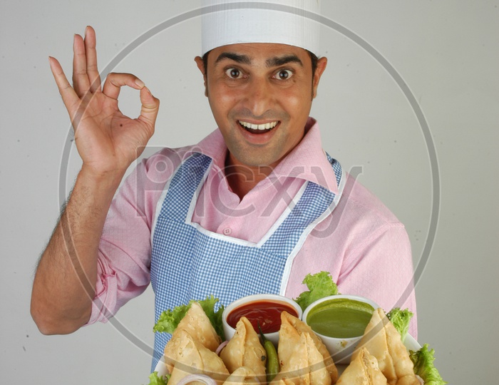 Image of An Indian Chef In Kitchen Apron And Cap Holding Samosas Plate ...