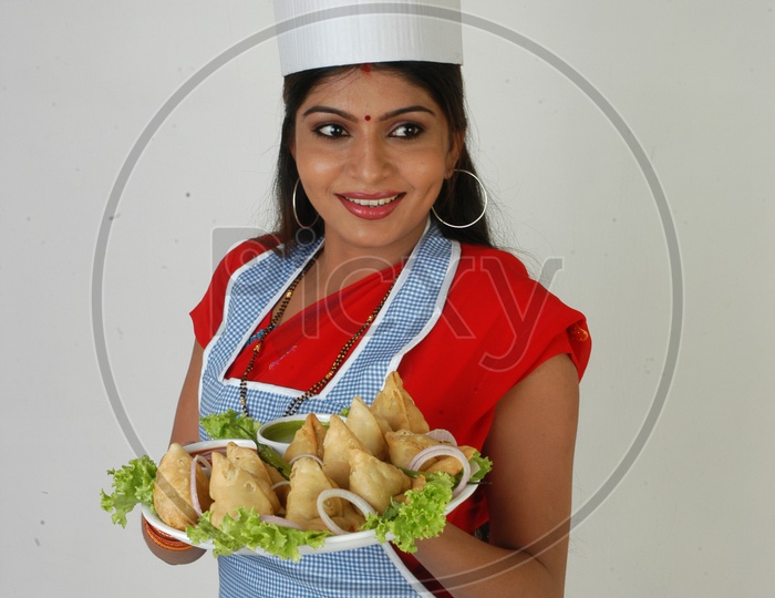 Image of An Indian Woman Chef In Kitchen Apron And Cap Holding Samosas ...