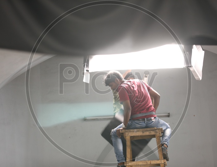 Image of Electrician Repairing The Light By Sitting on a Long Stool Or ...