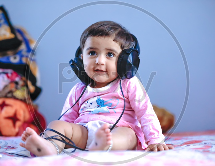 Image of Cute Indian Baby Girl Listening Music In Headphones-OQ346649-Picxy