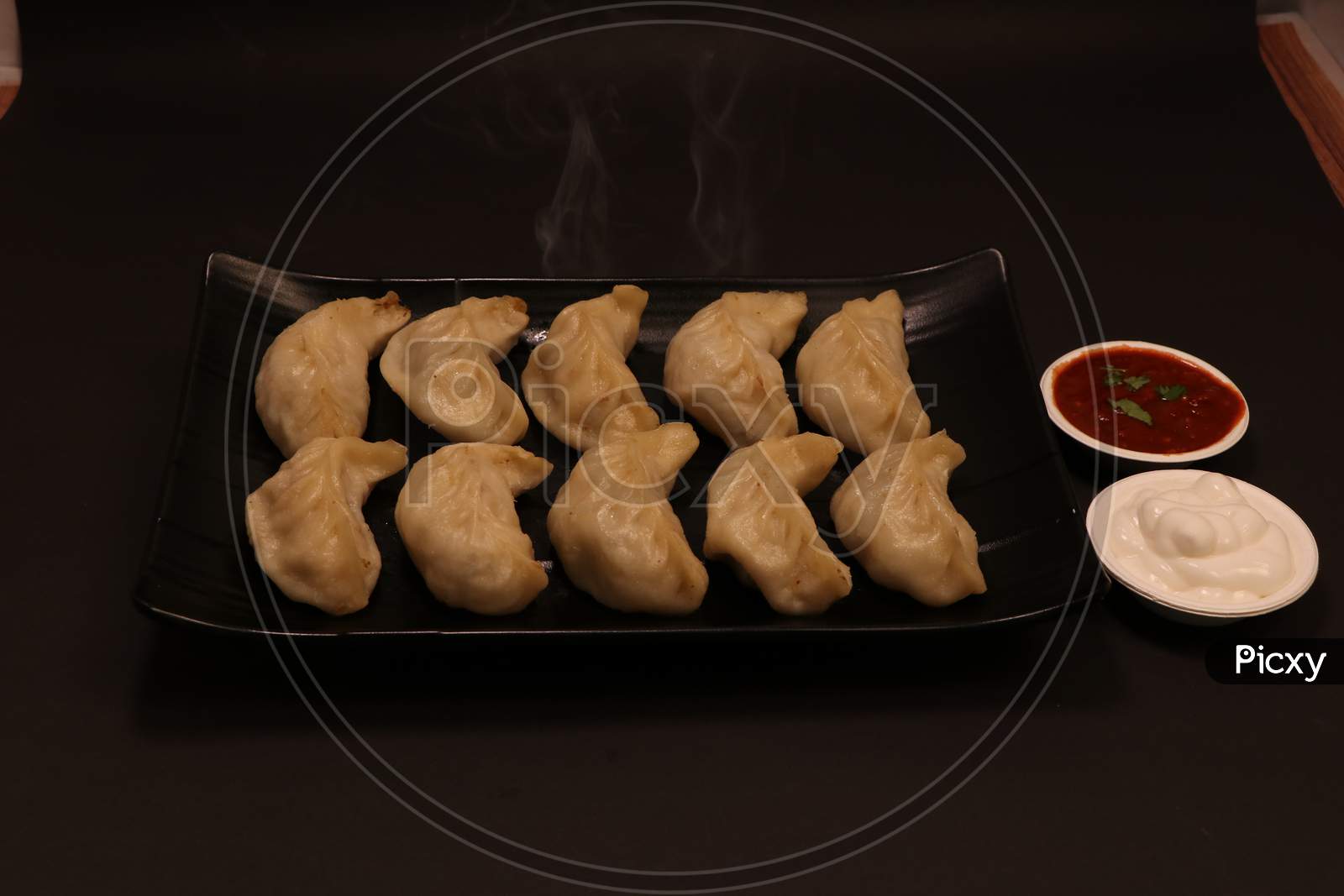 Image of Steam Momos in black Plate with red chatni and marination ...