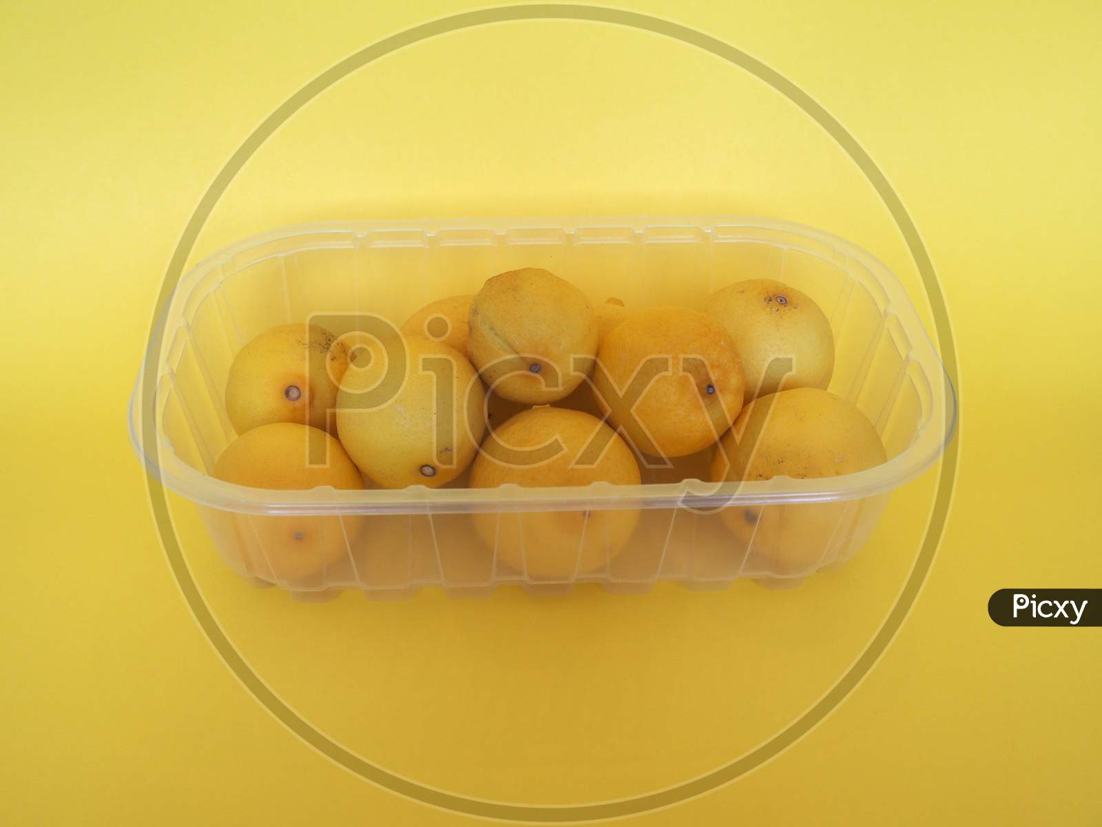 Image of Lemon Fruits In Plastic Box Over Yellow Background-EL849255-Picxy